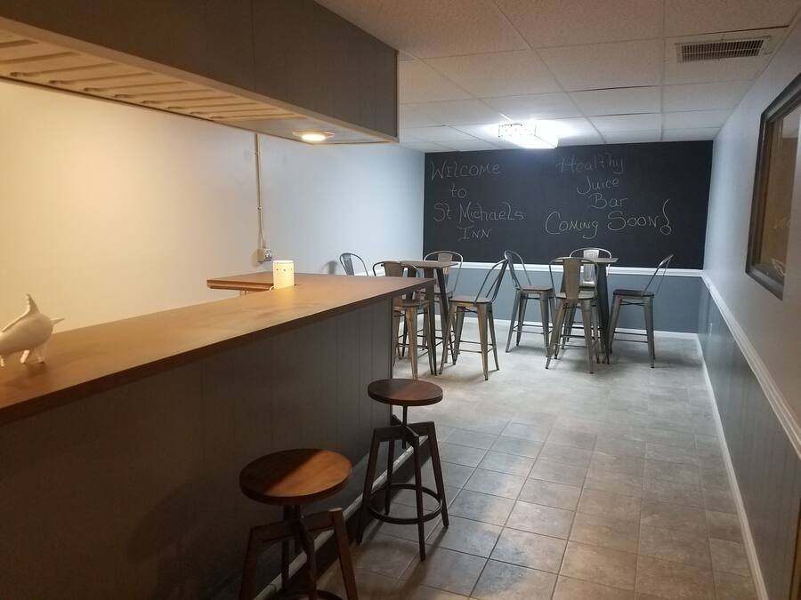 Uma área de bar com banquetas, um balcão de madeira e uma lousa com escrita.
