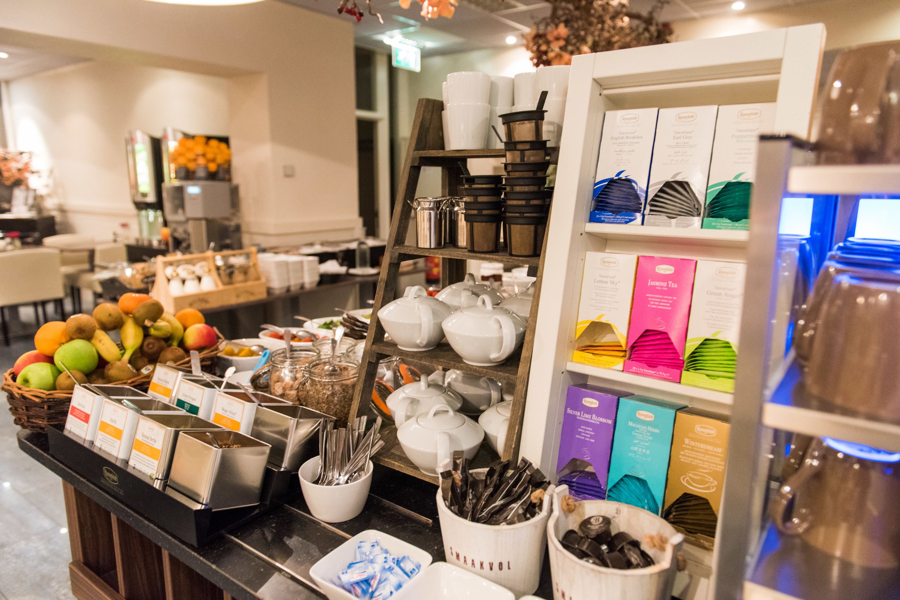 Uma área de buffet com diversos alimentos, utensílios e dispensadores de bebidas.