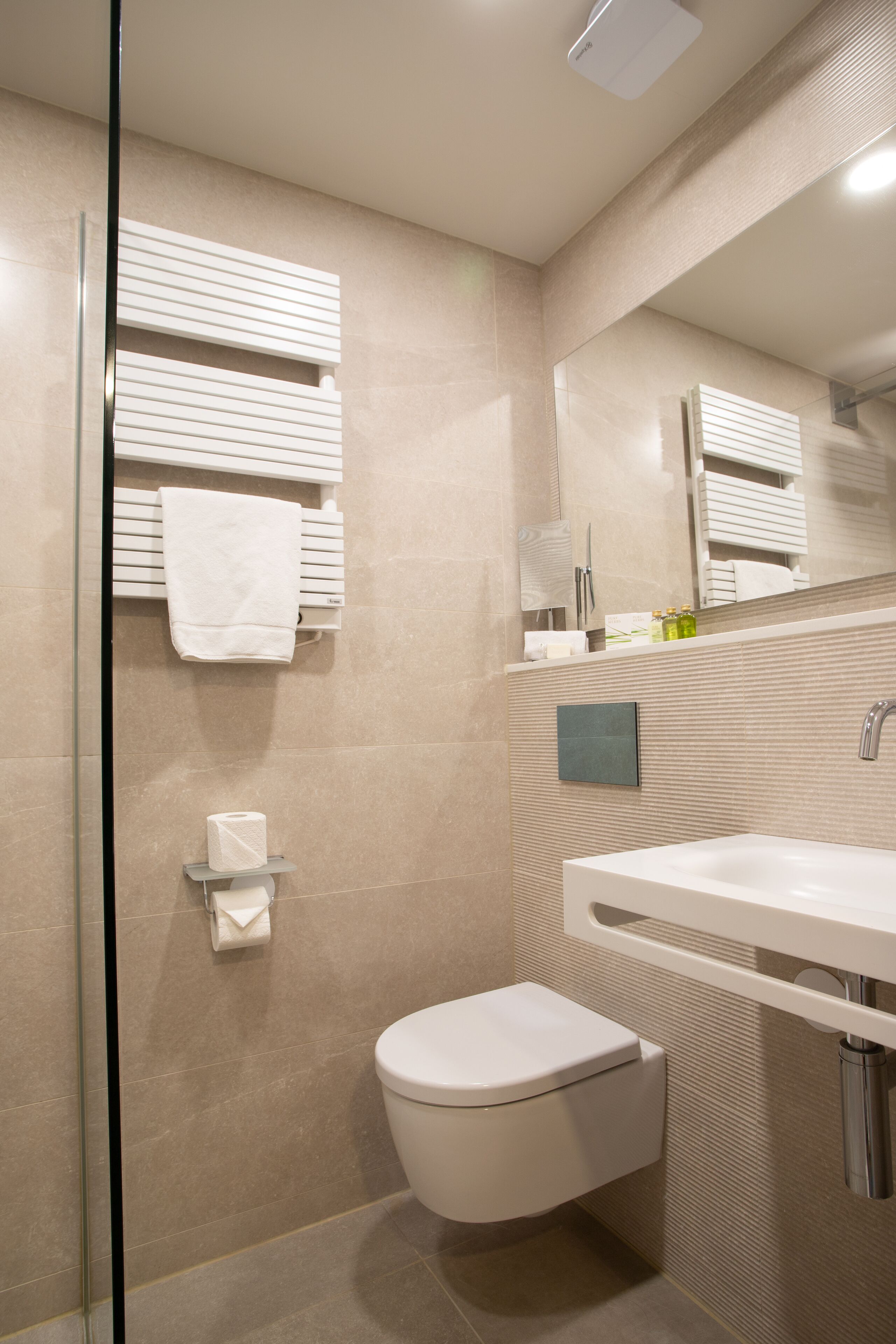 Um banheiro moderno com box de vidro, vaso sanitário branco, pia com espelho acima e porta-toalhas na parede.