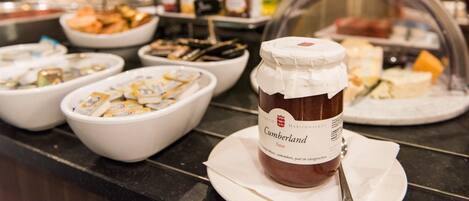 Buffet com diversos tipos de comida, incluindo um pote de Cumberland Saus, recipientes com alimentos e uma vitrine de vidro.