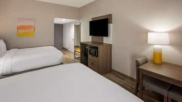 Quarto de hotel com duas camas, televisão, escrivaninha com abajur e um quadro na parede.