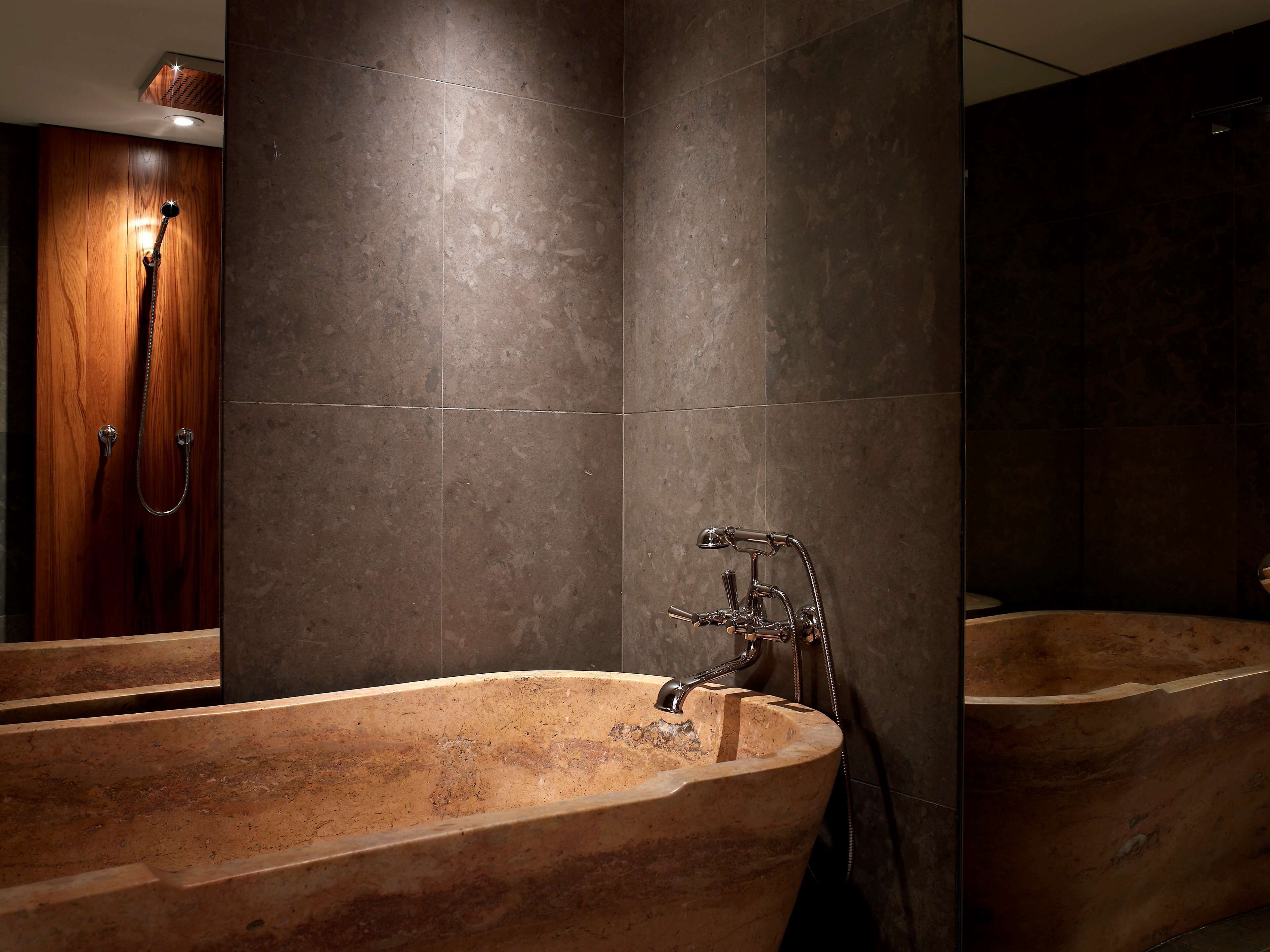 Um banheiro moderno com uma banheira independente, porta de madeira e paredes revestidas de azulejos escuros.