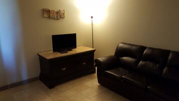 Uma sala de estar com televisão de tela plana em um armário de madeira, sofá de couro preto e abajur.