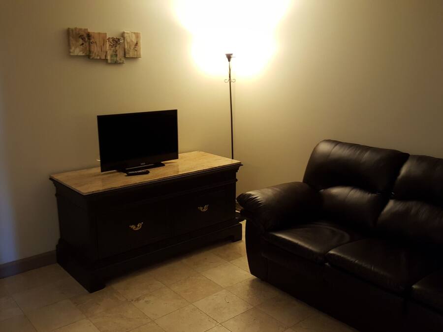 Uma sala de estar com televisão de tela plana em um armário de madeira, sofá de couro preto e abajur.