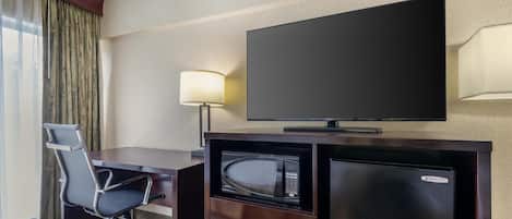Quarto de hotel com secretária, cadeira, televisão e minibar.
