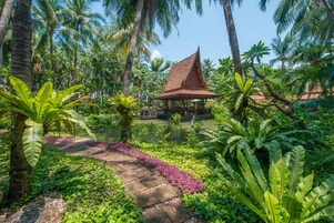 Um resort tropical com uma estrutura tradicional de telhado de palha, rodeado por vegetação exuberante e palmeiras.