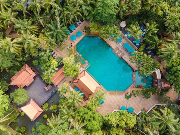 Vista aérea de um resort com uma piscina central, rodeada por palmeiras e áreas de descanso.