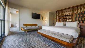 Quarto de hotel moderno com uma cama grande, um sofá, uma TV e um painel decorativo na parede.