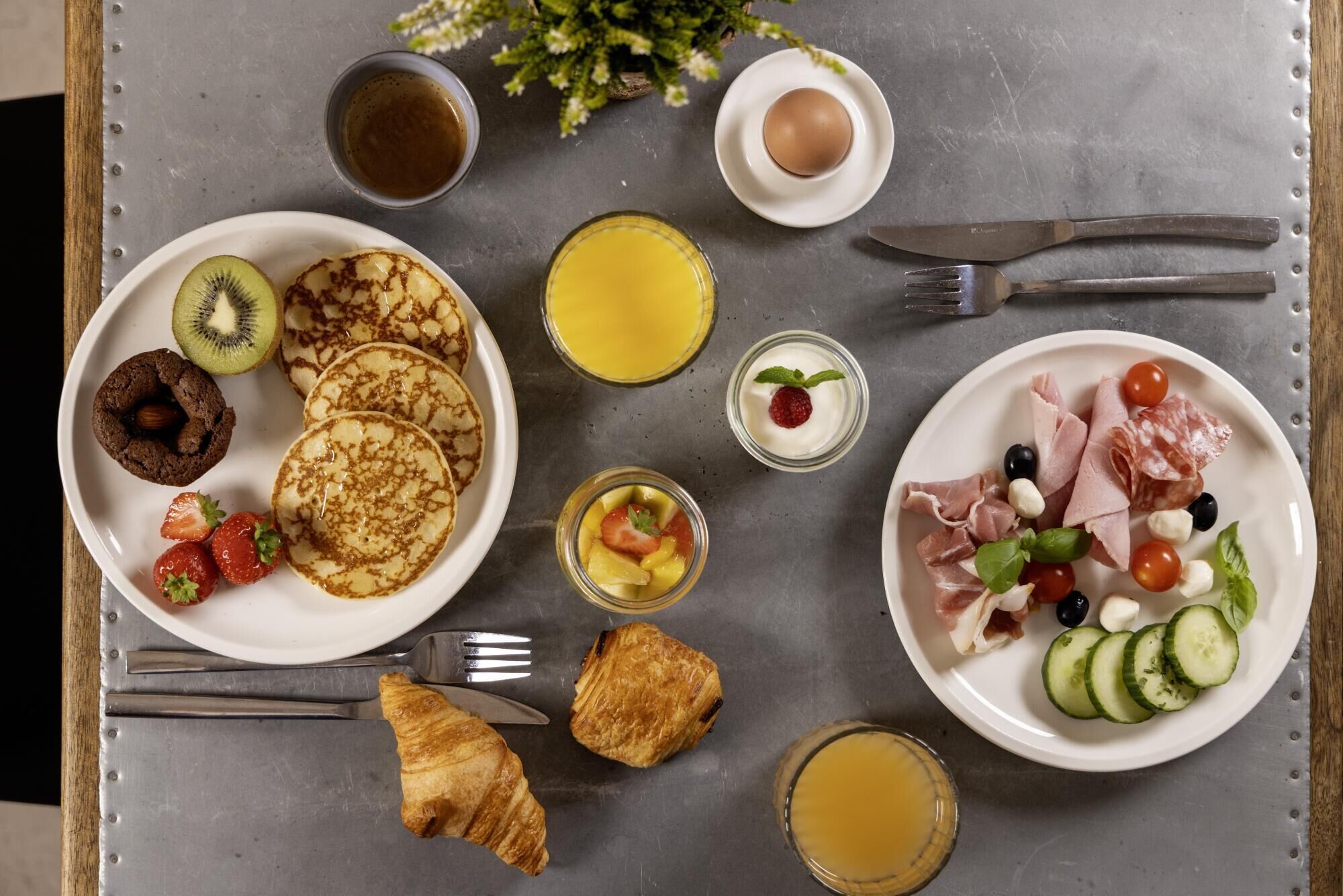 Bandeja de café da manhã com panquecas, kiwi, morangos, croissants e um prato de carnes e queijos.
