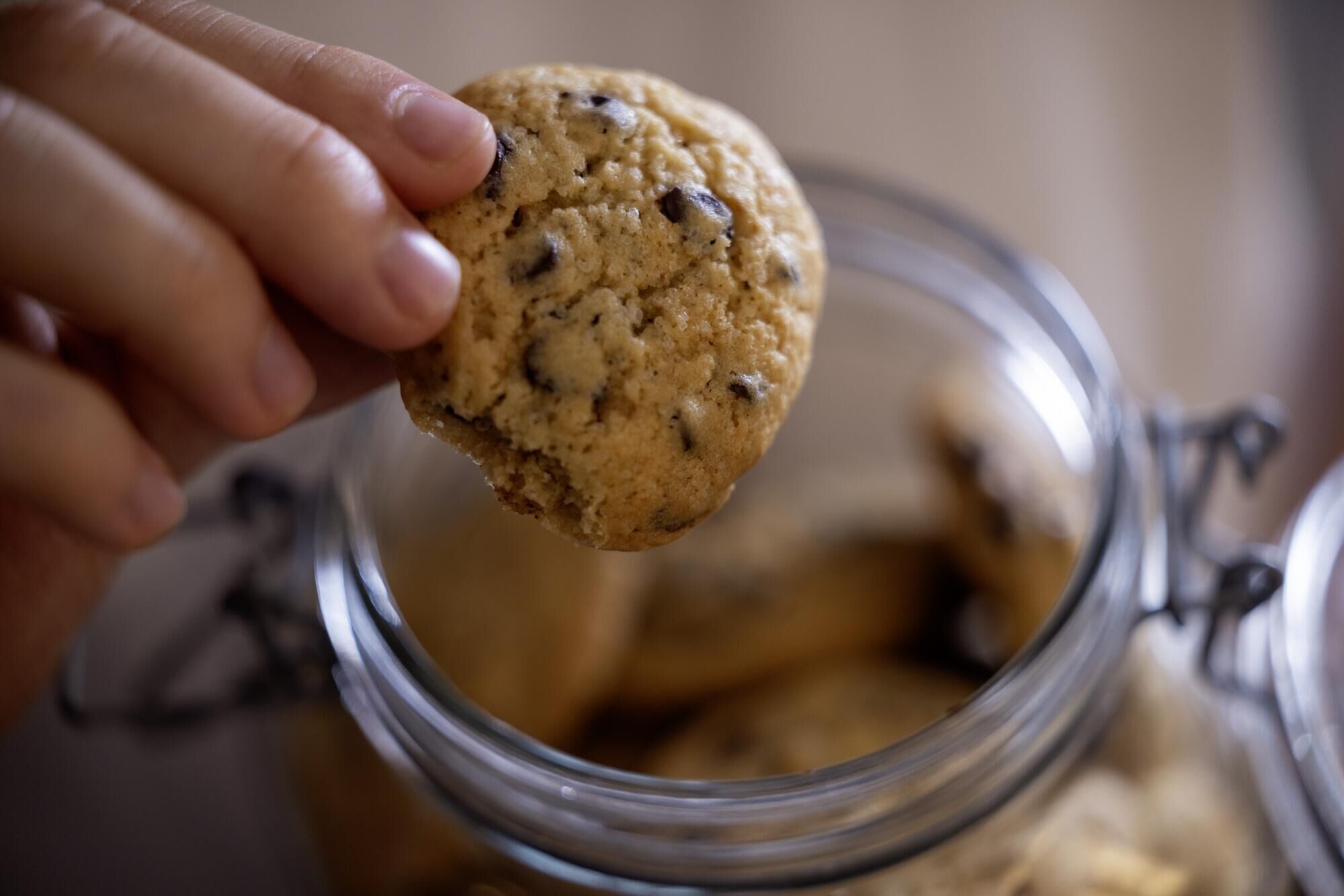 Uma mão segurando um biscoito sobre um pote cheio de biscoitos.