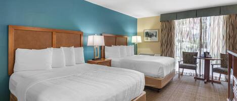 Quarto de hotel com duas camas, uma pequena mesa com cadeiras e uma janela com cortinas.