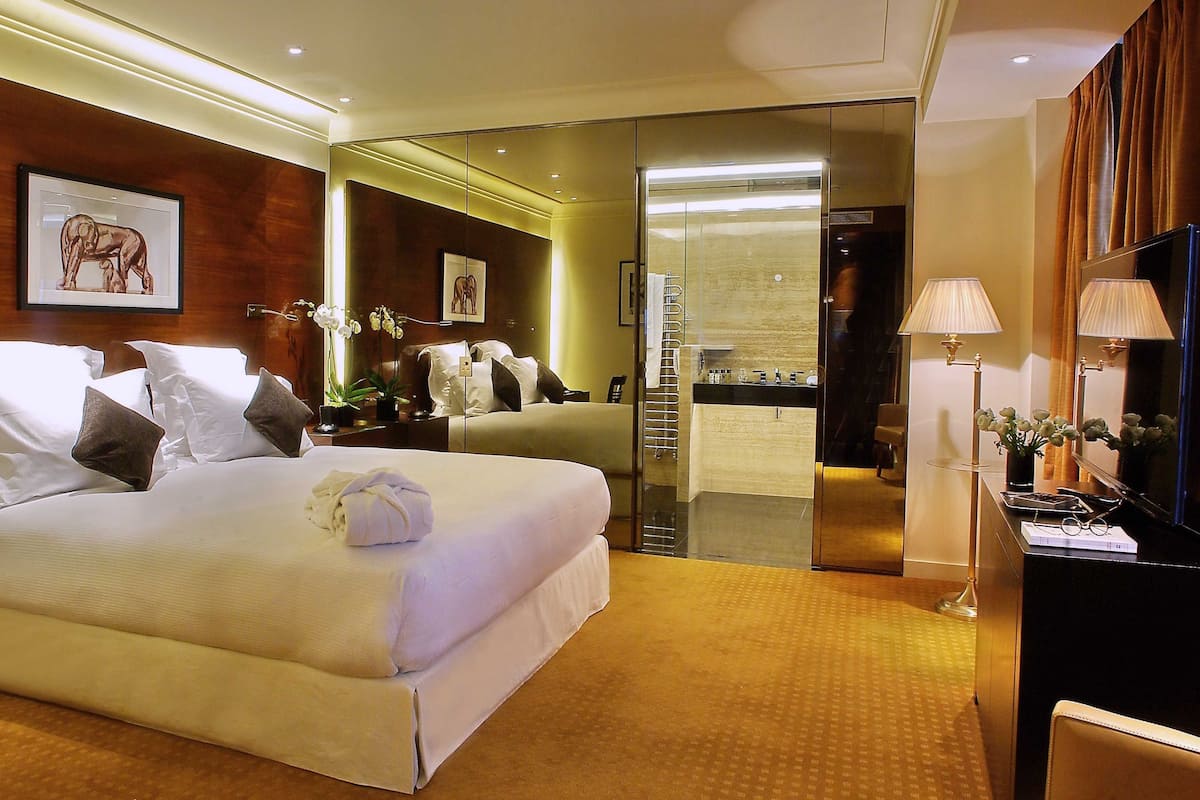 Quarto de hotel com uma cama grande, uma escrivaninha com luminária e um espelho.