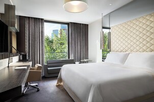 Quarto de hotel moderno com uma cama grande, uma escrivaninha com cadeira, um sofá e vista para o verde lá fora.