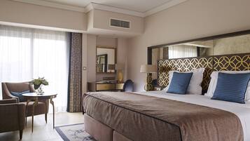 Quarto de hotel com uma cama grande, uma escrivaninha, uma cadeira e uma pequena mesa com uma planta.