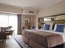 Quarto de hotel com uma cama grande, uma escrivaninha, uma cadeira e uma pequena mesa com uma planta.