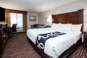 Quarto de hotel com uma cama grande, uma mesa com televisão de tela plana, um sofá e uma janela com cortinas.