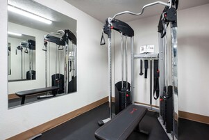 Uma academia com equipamentos de exercícios, um banco e um espelho.