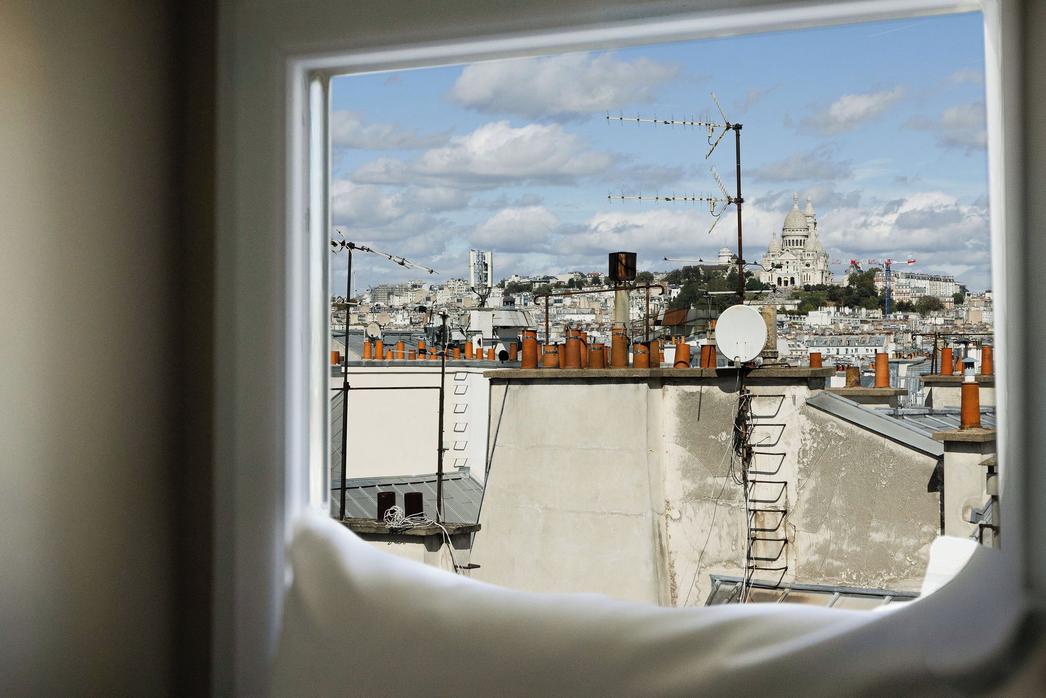 Vista da janela sobre uma paisagem urbana com edifícios, uma estrutura em forma de cúpula e céu claro.