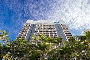 Hotel alto com várias varandas, cercado por palmeiras.