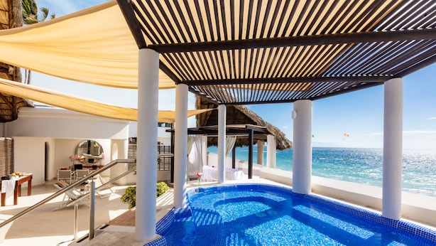 Área da piscina com vista para o oceano, espaço de estar coberto e escadaria que leva a um terraço.