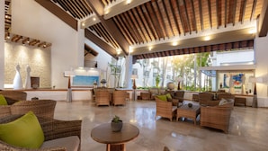 Um hall amplo com móveis de vime, uma parede de pedra e vista para o exterior.