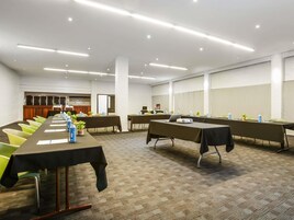 Uma sala de conferências com mesas compridas, cadeiras e um projetor.