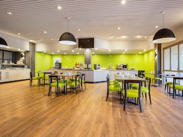 Restaurante moderno com parede em padrão losango verde, piso de madeira e cadeiras verdes.