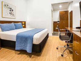 Quarto de hotel com cama, escrivaninha com cadeira, guarda-roupa e um quadro na parede.
