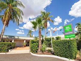 Uma área de recepção de hotel com palmeiras, céu claro e uma placa para hotéis ibis Styles.