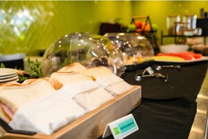 Disposição de buffet com alimentos cobertos e placa indicando opções vegetarianas.