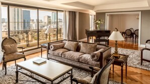 Uma sala de estar espaçosa com uma grande janela que oferece vista para a cidade, um sofá confortável, uma mesa de centro e um piano ao fundo.
