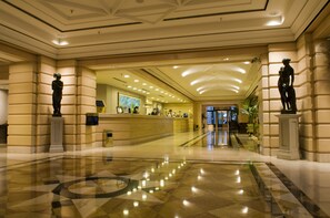 Um hall amplo com piso de mármore polido, um balcão de recepção e duas estátuas em pedestais.