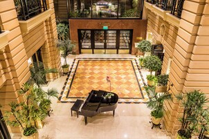 Um hall de hotel com piso xadrez, um piano e plantas em vasos.