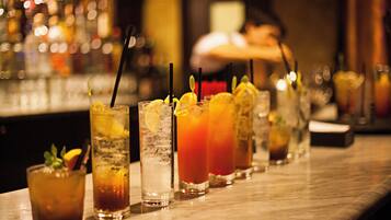 Balcão de bar com diversas bebidas, incluindo cocktails e opções não alcoólicas, com um fundo desfocado que sugere um ambiente de bar movimentado.