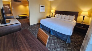 Quarto de hotel com cama, abajures, escrivaninha com computador, cadeira e carpete estampado.