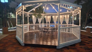 Um gazebo com grade branca, uma mesa redonda e cadeiras.