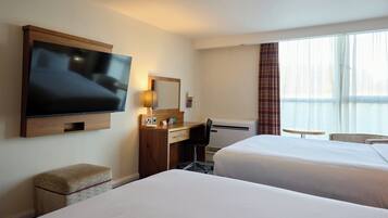 Quarto de hotel com duas camas, uma escrivaninha, uma cadeira, uma televisão e uma janela com cortinas.