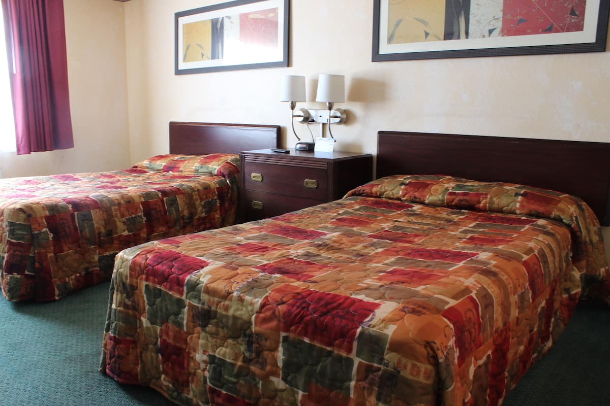 Quarto de hotel com duas camas de solteiro, mesa de cabeceira com abajur e luminária na parede.