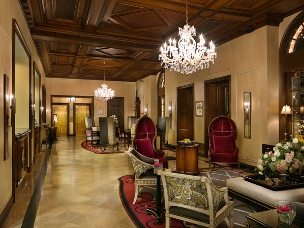 Um amplo hall de entrada com lustre, poltronas estofadas em vermelho e um balcão de recepção.
