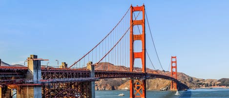 Uma grande ponte suspensa com uma torre notável e cabos, atravessando um corpo de água com colinas ao fundo.