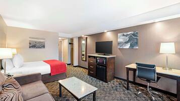 Quarto de hotel com uma cama, uma escrivaninha, uma cadeira, uma televisão e um micro-ondas.