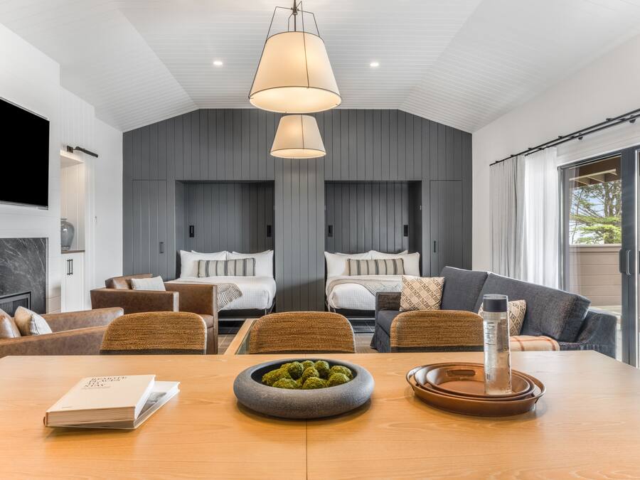 Uma sala de estar moderna com uma grande mesa de madeira, dois sofás e uma TV fixada na parede.