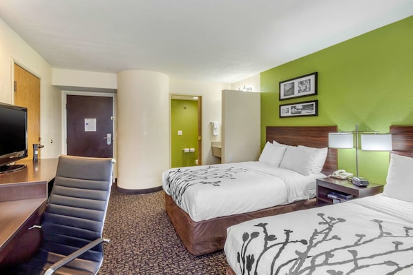 Quarto de hotel com uma cama, uma escrivaninha com computador, uma cadeira e uma televisão.