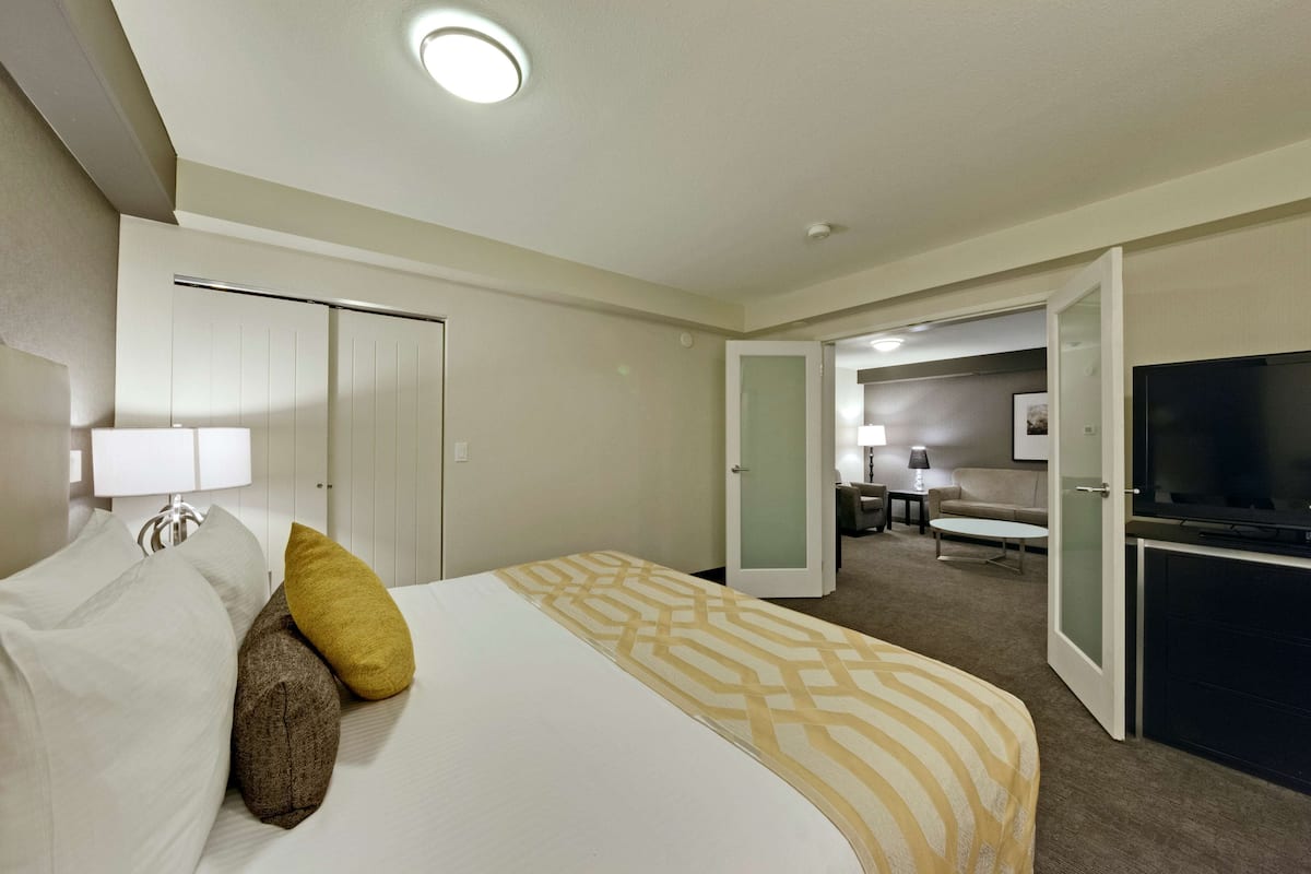 Quarto de hotel com uma cama, televisão, escrivaninha e porta que dá para outro espaço.