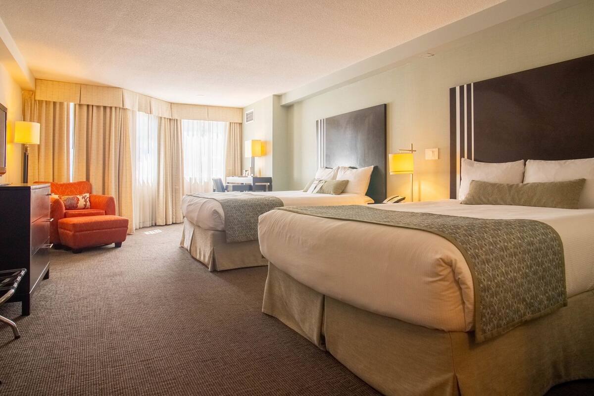 Quarto de hotel com duas camas, uma escrivaninha, uma cadeira e uma televisão.