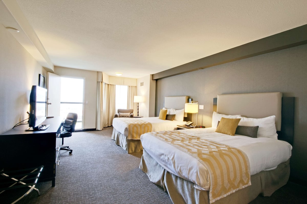 Quarto de hotel com duas camas, uma escrivaninha, uma cadeira e uma televisão.