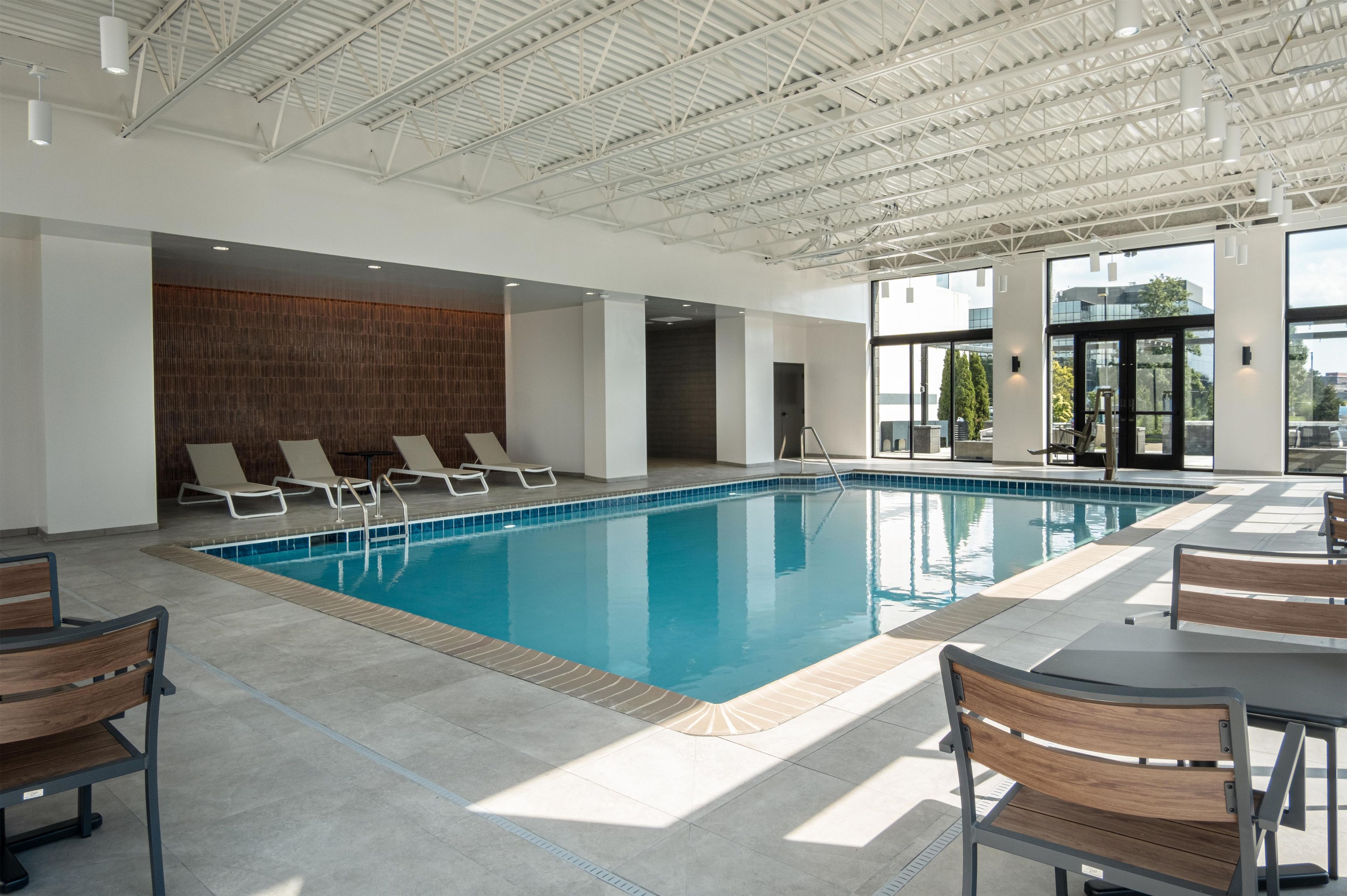 Piscina interior moderna com água azul cristalina, rodeada por espreguiçadeiras e mesas.