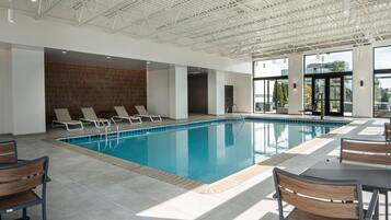 Piscina interior moderna com água azul cristalina, rodeada por espreguiçadeiras e mesas.