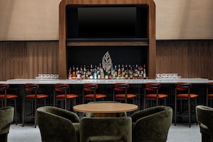 Uma área de bar com balcão comprido, vários bancos e uma mesa redonda.