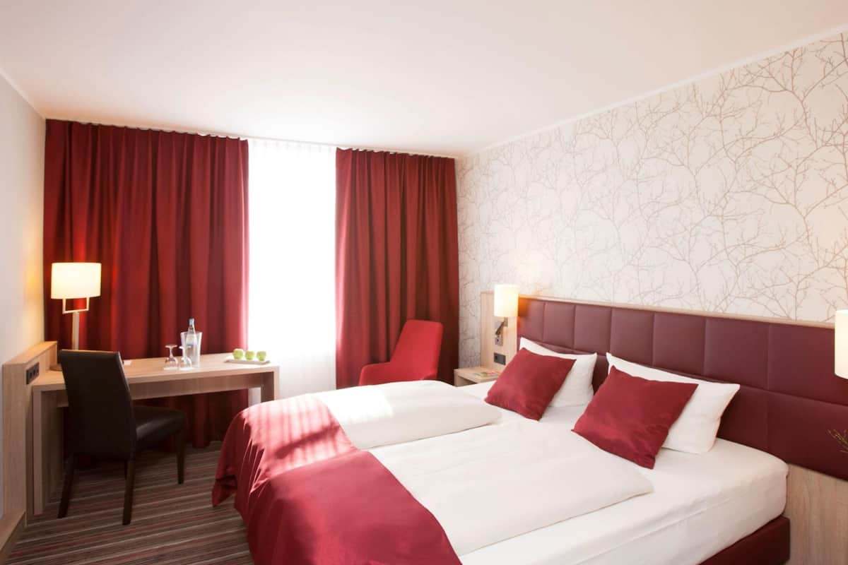 Quarto de hotel com cama, escrivaninha, cadeira e duas luminárias de cabeceira.